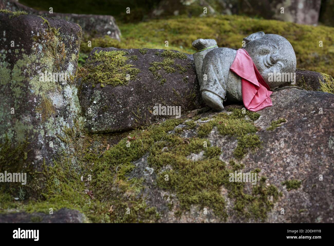 Horizontal close-up shot of a smiling stone Jizo statue laying over a ...