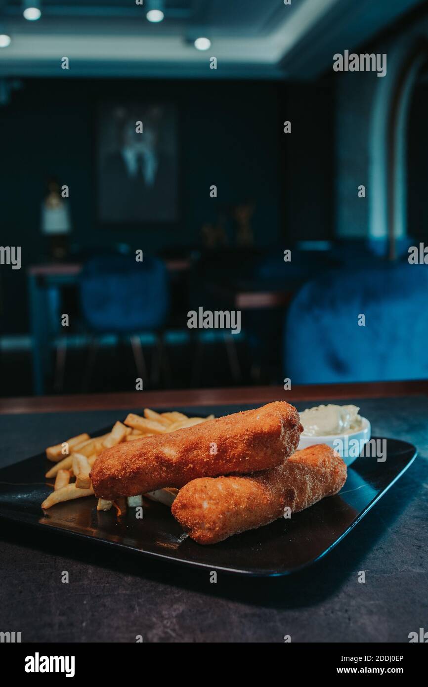 A closeup of fried cheese sticks with french fries and sauce on a plate ...