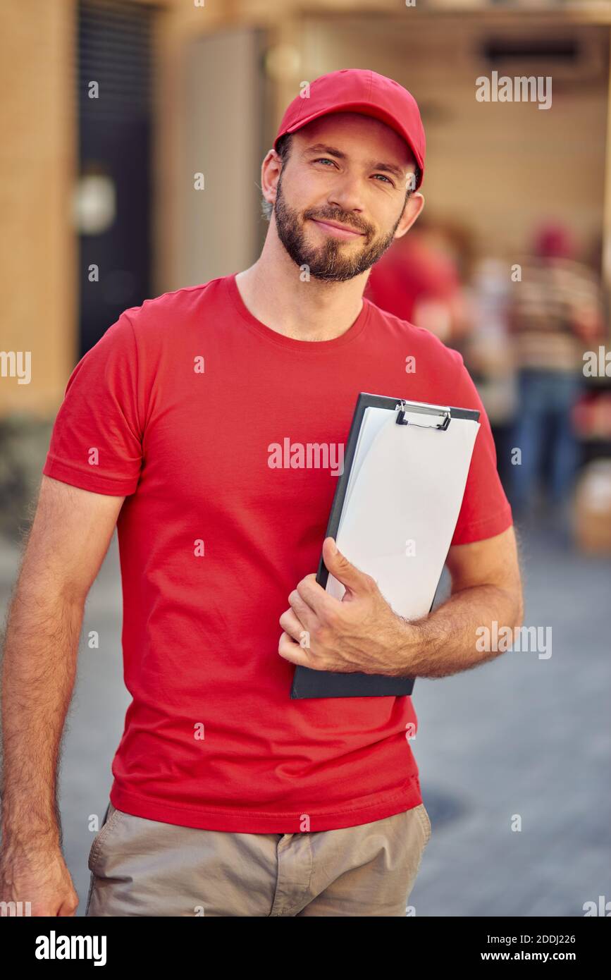 Young happy caucasian male courier in uniform holding folder with ...
