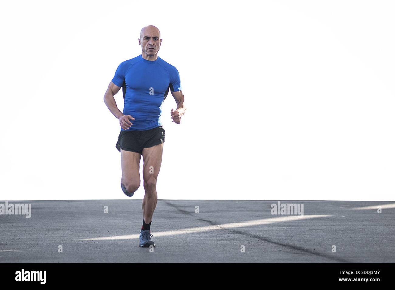 A bald muscular Caucasian athlete running against a white clear sky ...