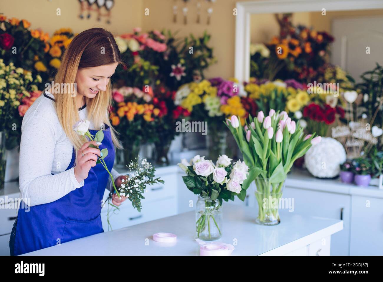 A beautiful smiling florist creates a composition of white flowers in a ...