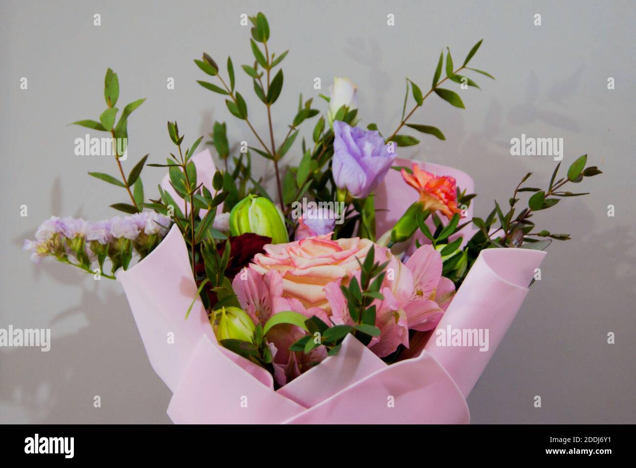 A delicate bouquet of different flowers in a light pink wrapper stands ...