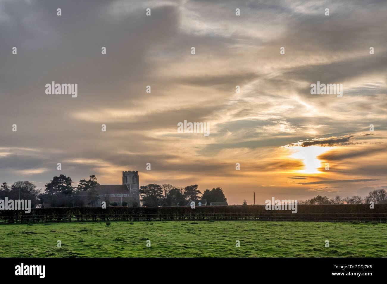 Sun setting behind the Church of St Peter, Wolferton across fields on ...