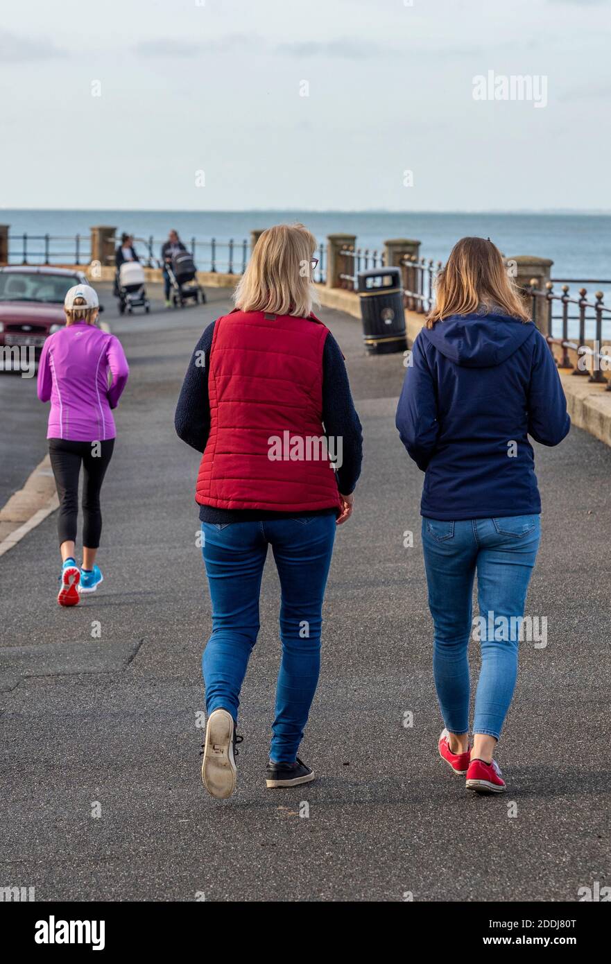 two women walking and talking together along the seafront at cowes on ...
