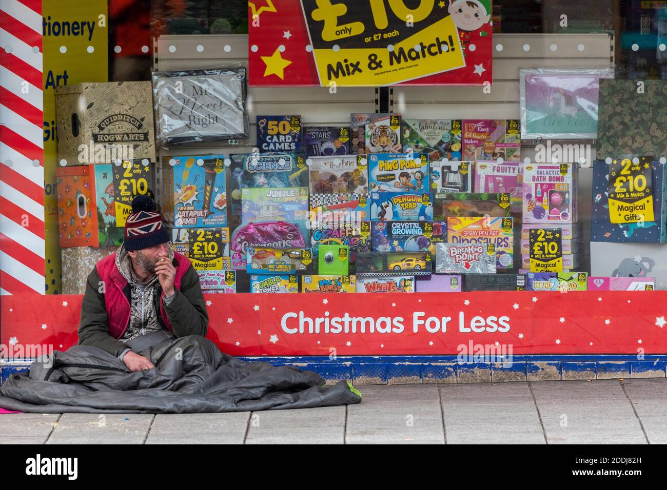 homeless man sitting on the floor or pavement outside of a shop selling ...