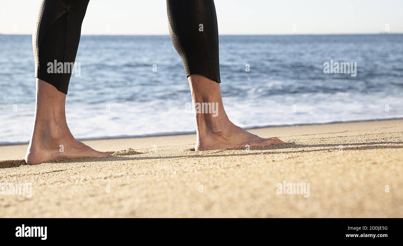 A closeup of a male Caucasian athletic swimmer's feet stepping on beach ...