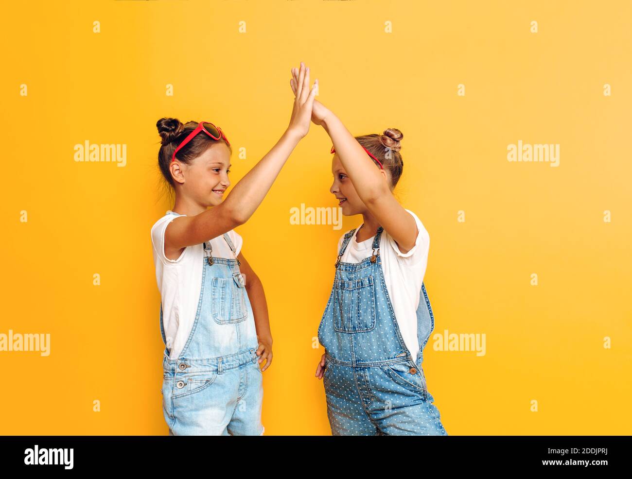 Two teenage girls, stylish friends, greet each other on a yellow ...