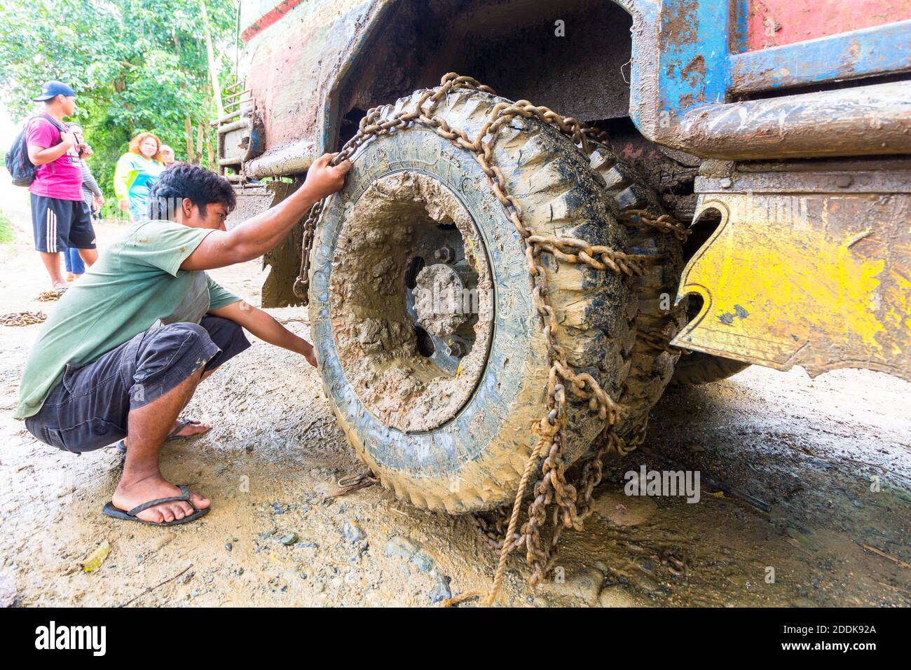 A jeepney driver putting on chains to the wheels before passing a muddy ...
