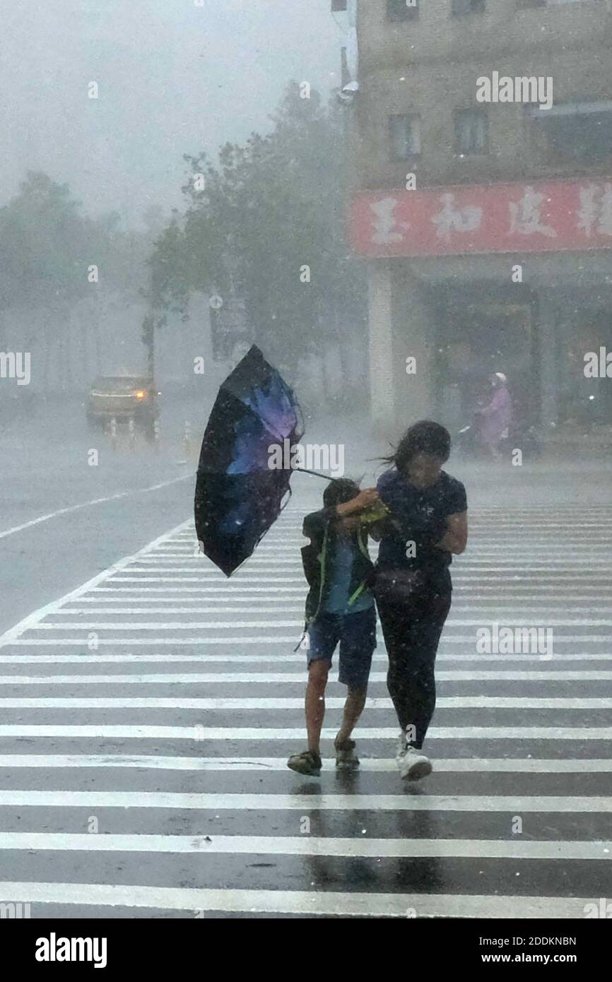 People struggle with heavy winds and rain while crossing the street as ...