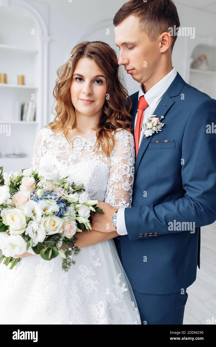 Beautiful bride in white dress and groom in suit, posing in white ...