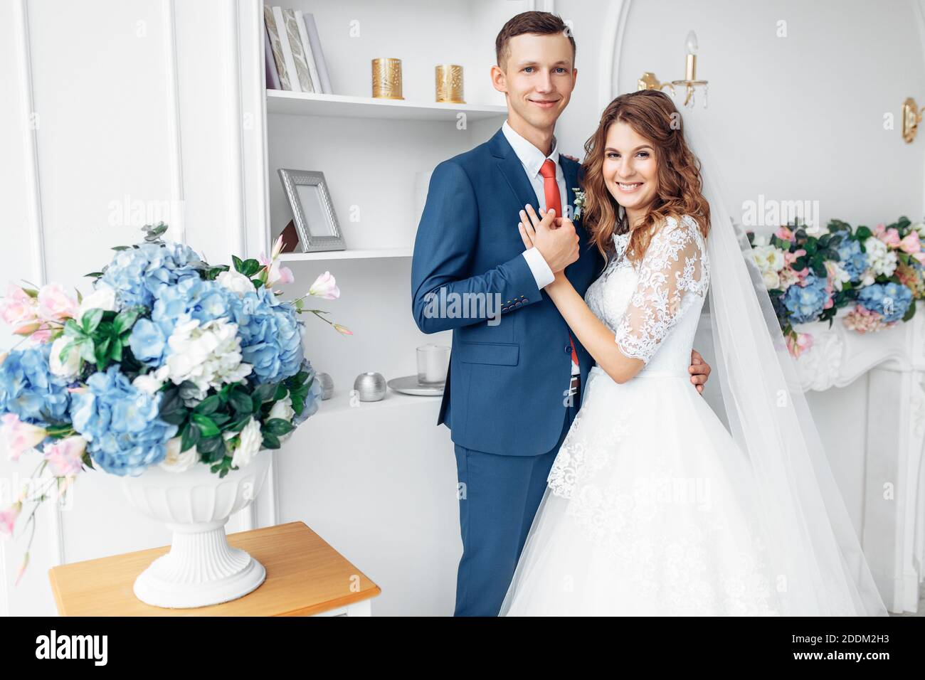 Beautiful bride in white dress and groom in suit, posing in white ...