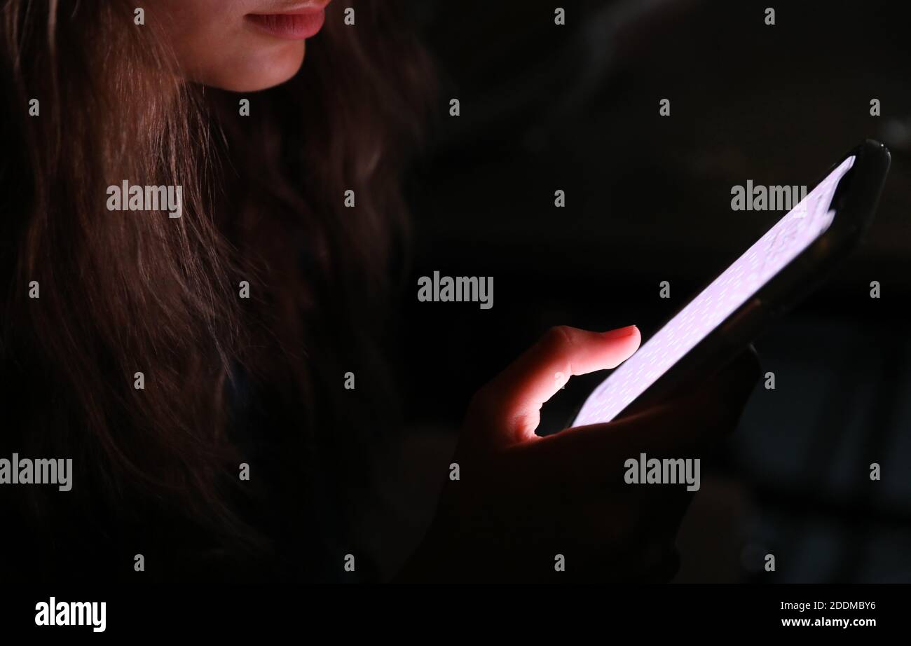 Person using a mobile cell phone at night in the dark. The glow of the ...