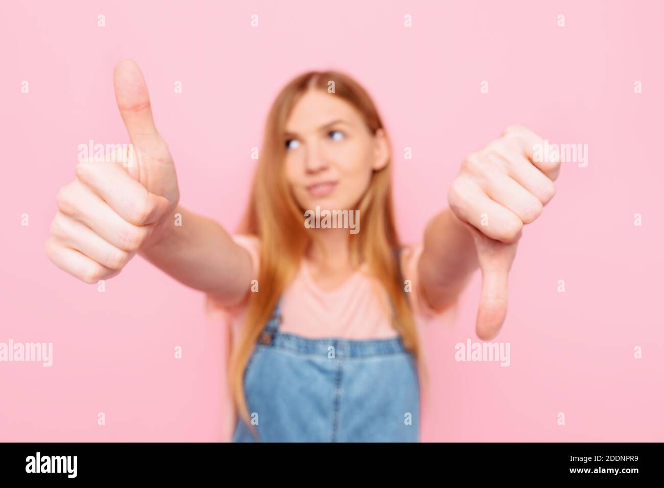 A young attractive stylish woman makes a good-bad sign. Undecided ...