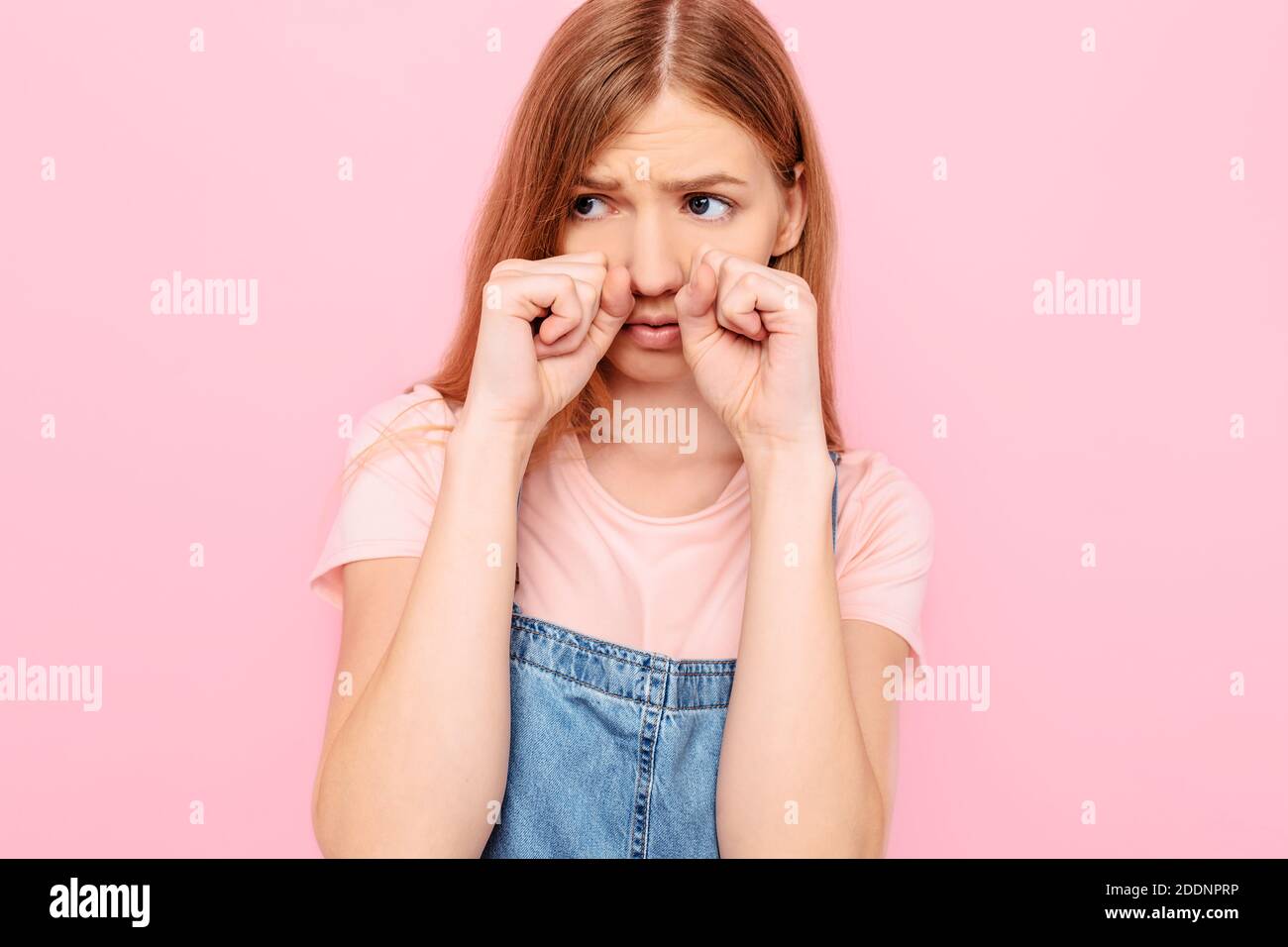 An aggrieved , crying young girl holding her hands near her eyes, on an ...