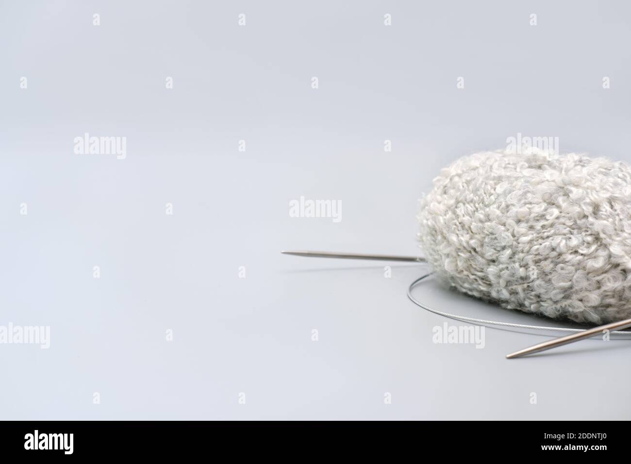 grey knitting yarn in a skein with needles on grey background ...