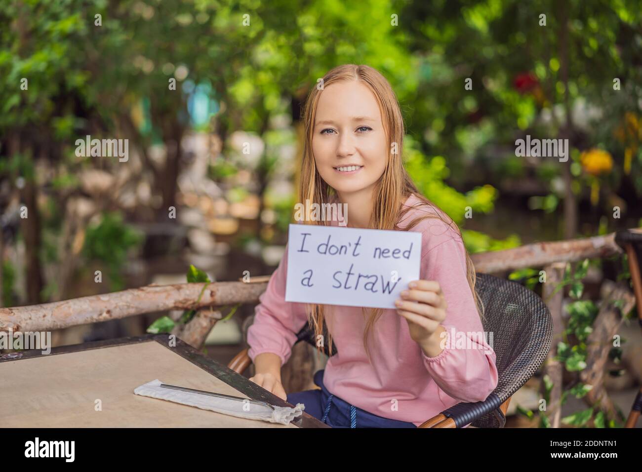 Young woman in a cafe shows a sign - I don't need a straw. No plastic ...