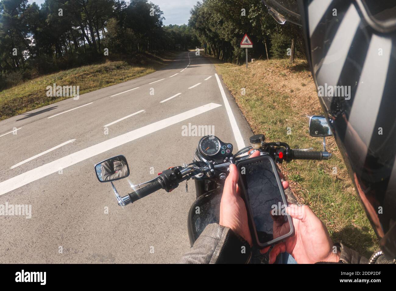 Motorbike rider on the edge of the road checking his mobile phone ...