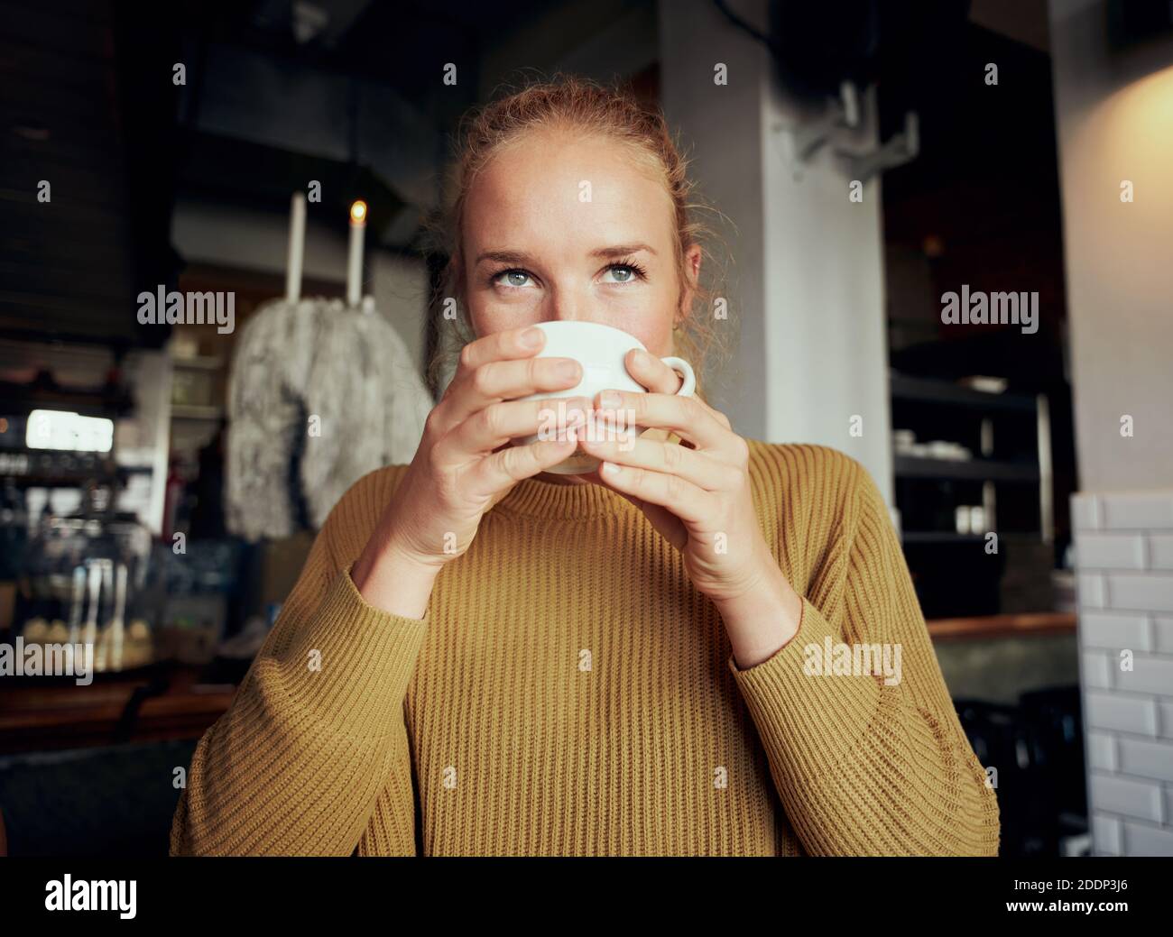 Young woman drinking coffee in cafeteria while looking away Stock Photo ...