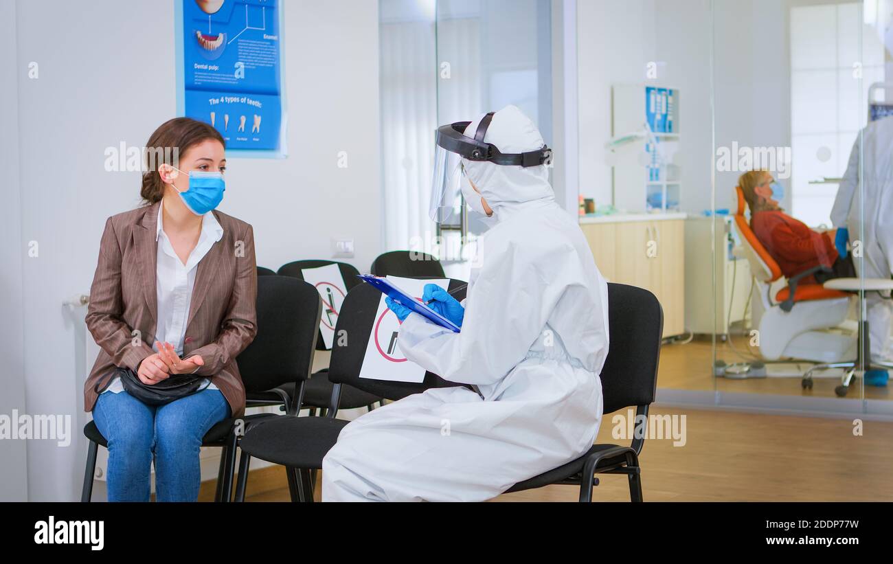 Stomatologist in protective suit reviewing registration form with ...