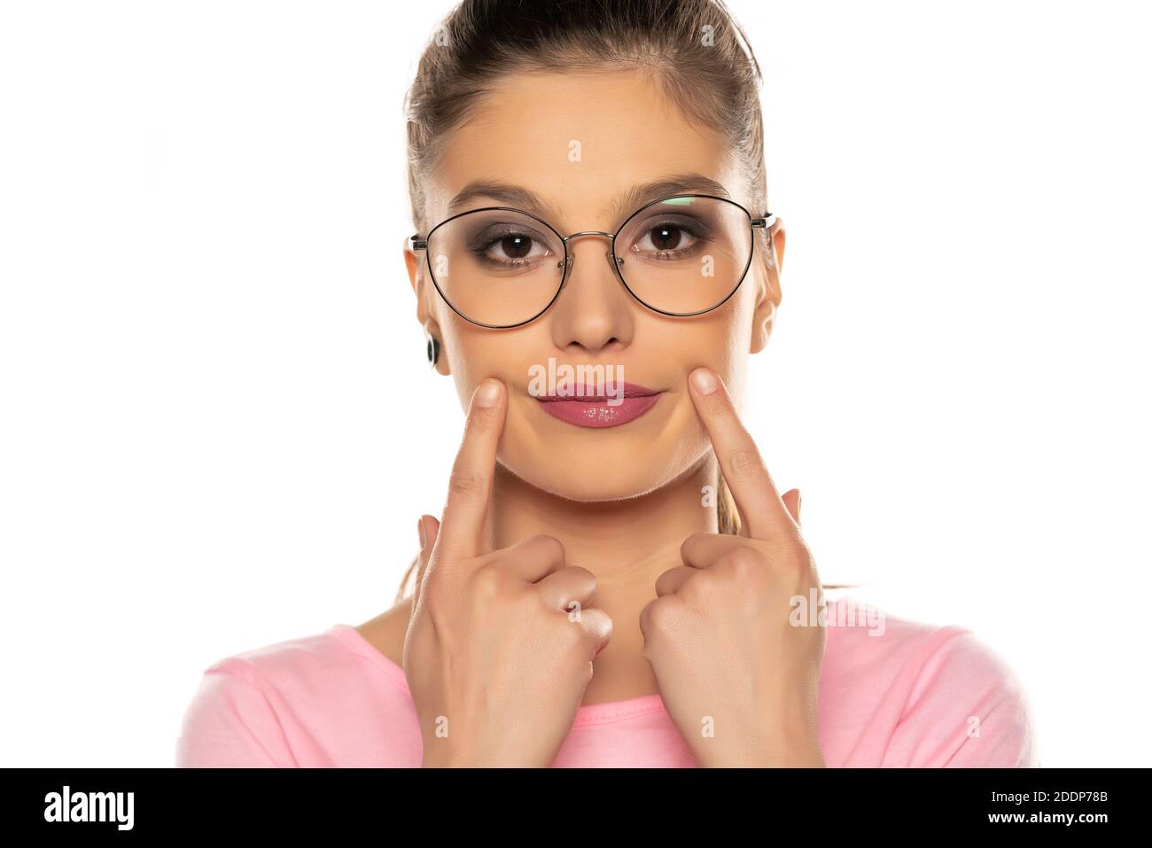 Portrait of young beautiful woman forcing her smile with her fingers on ...
