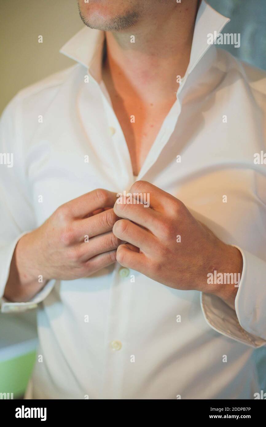 A man buttoning his white shirt in the morning, getting ready for work ...