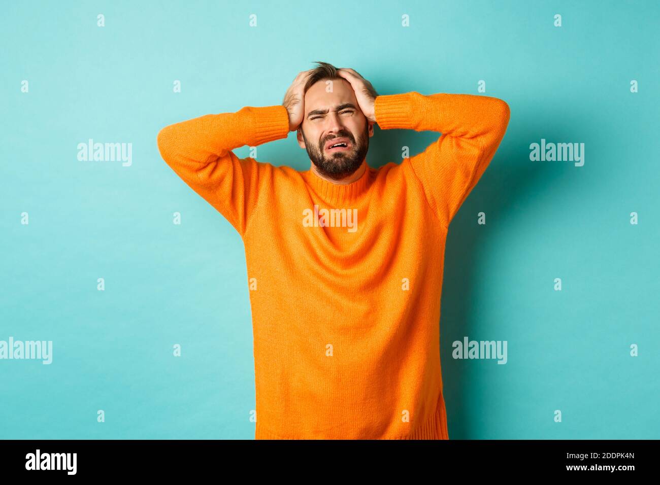 Image of frustrated man in orange sweater, holding hands on head and ...