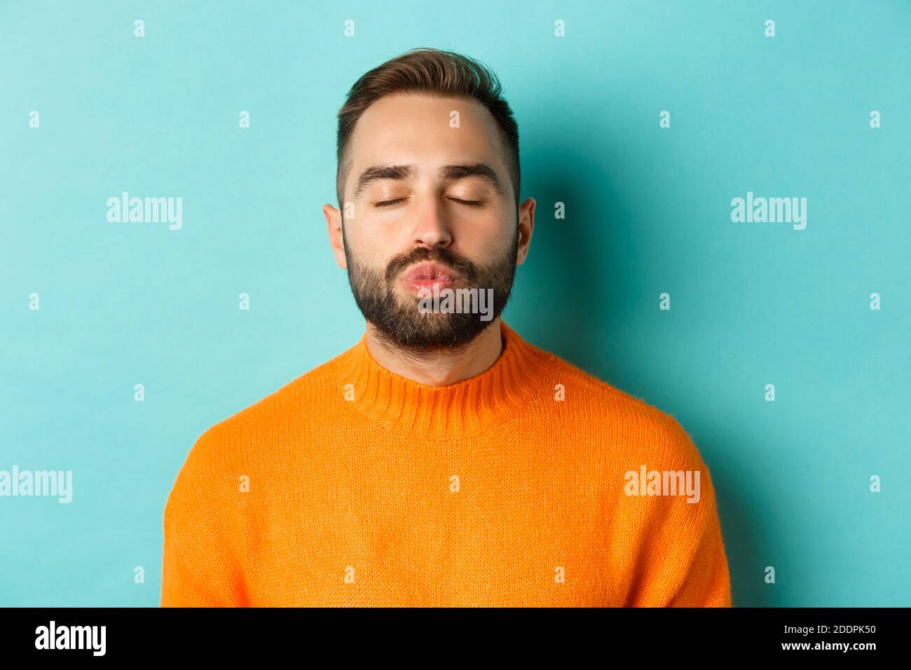 Close-up of young man in sweater pucker lips, close eyes and waiting ...