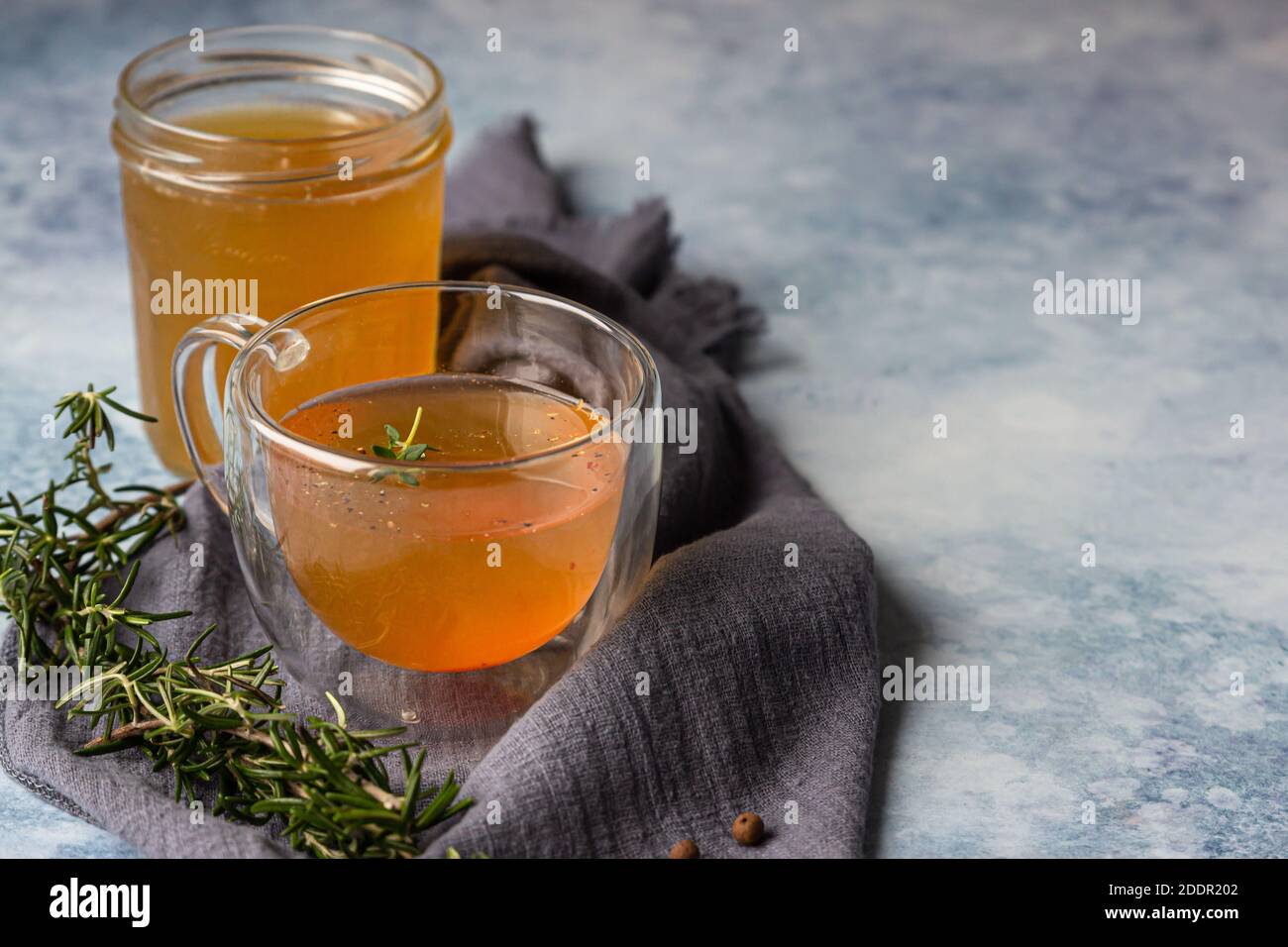 Bone or vegetable broth, bouillon in a glass mug and aromatic herbs on ...