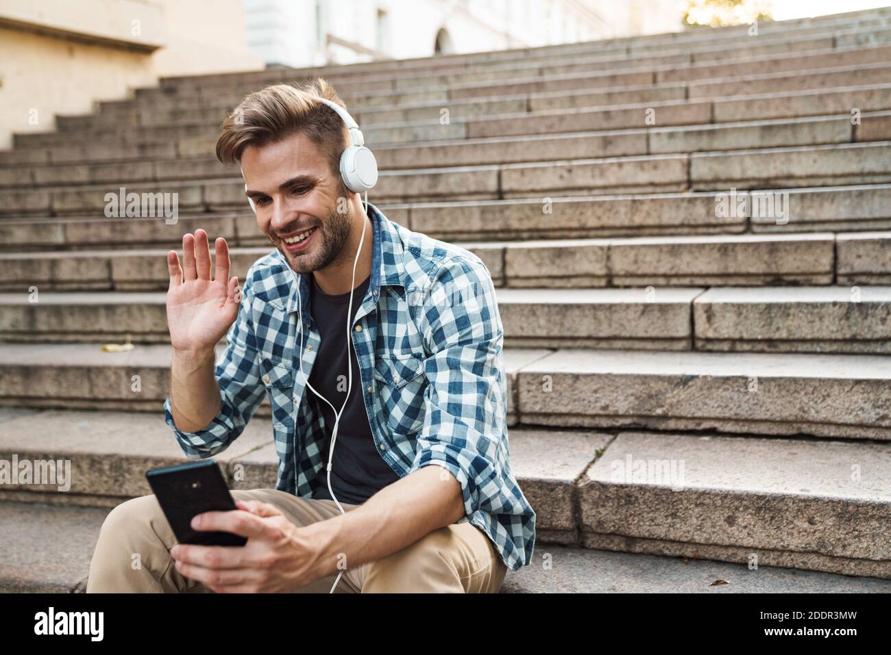 Handsome happy man video chatting on the phone while sitting on steps ...