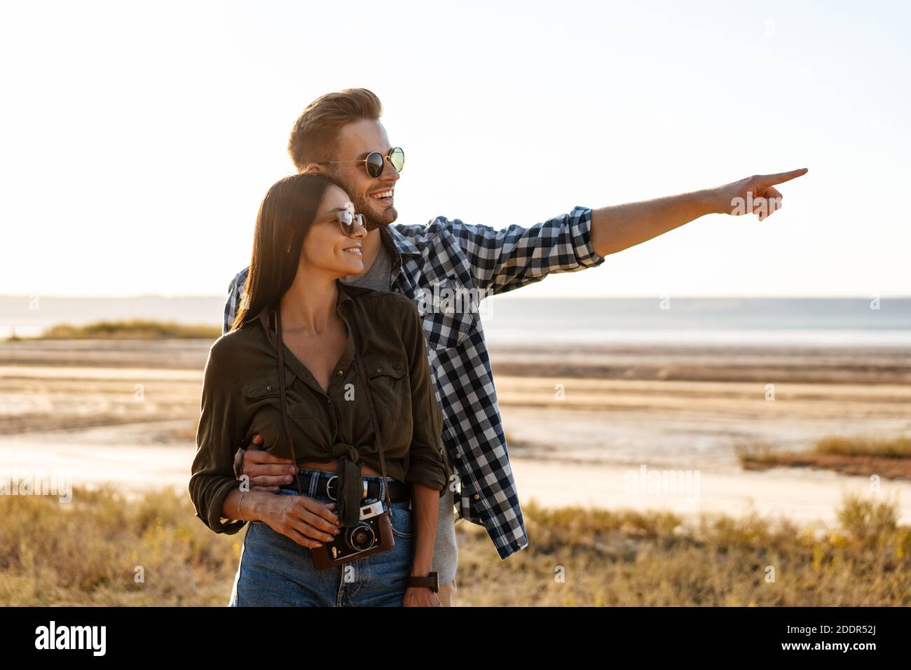 Beautiful happy couple hugging and pointing finger aside while ...
