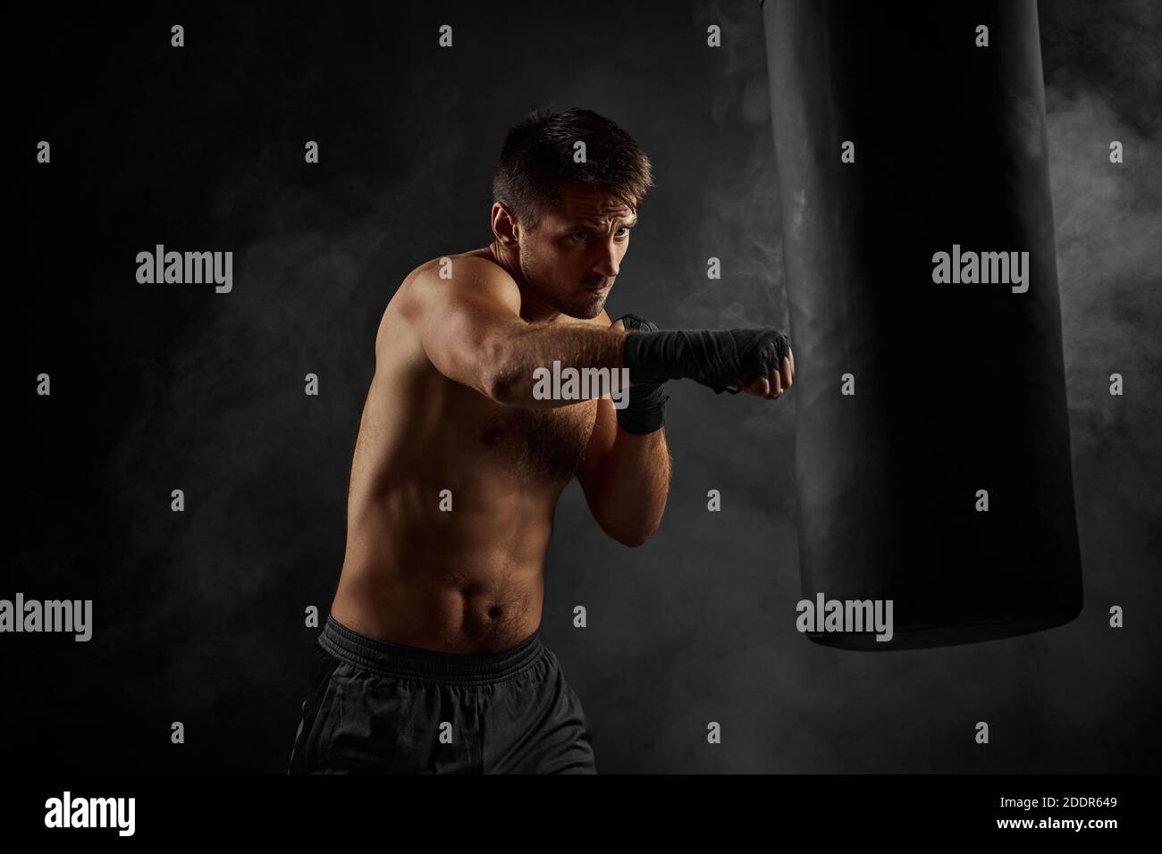 Male boxer training defense and attacks in boxing bag on black ...