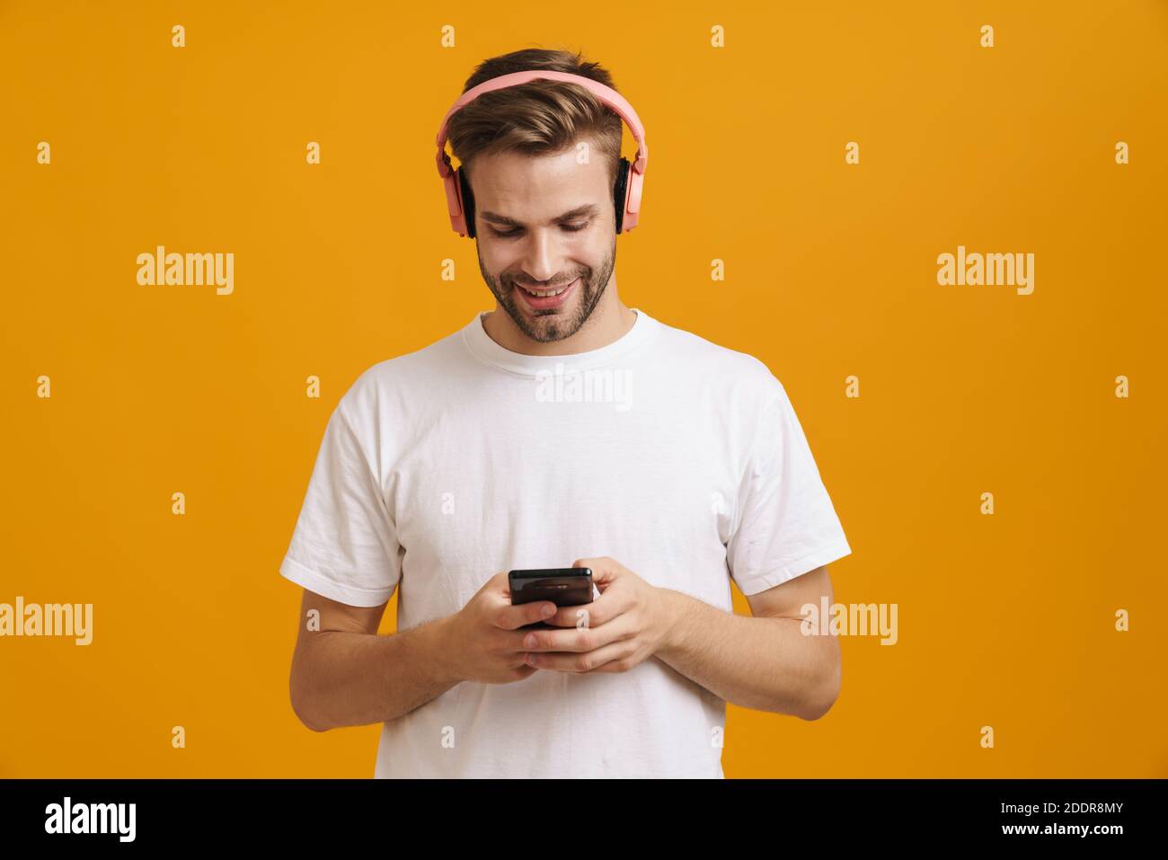 Photo of joyful handsome guy in headphones using mobile phone isolated ...