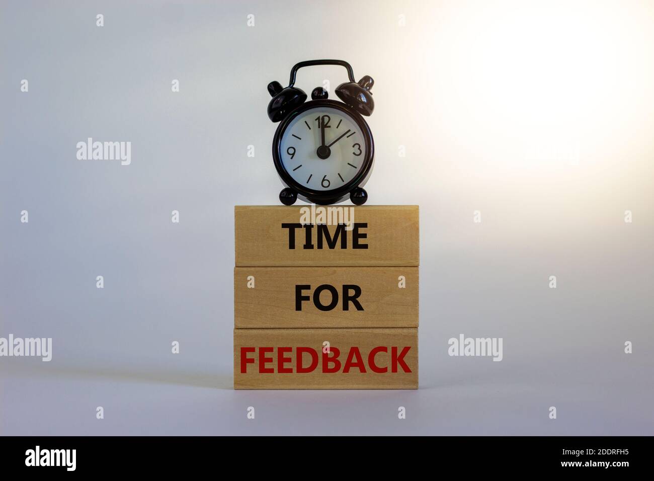 Wooden blocks with words 'time for feedback'. White table. Black alarm ...