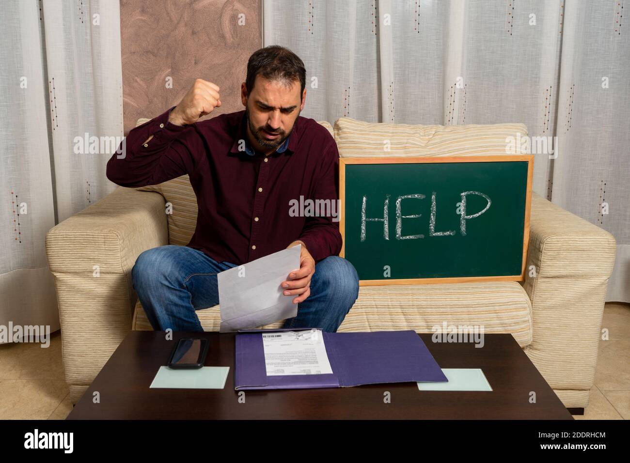 Desperate young man calculating household expenses sitting on the couch ...