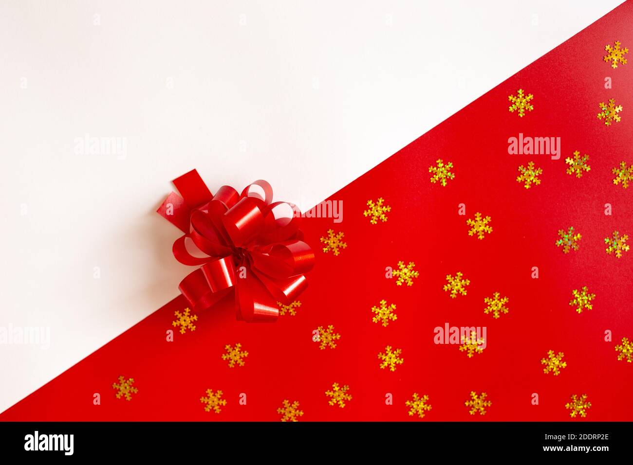 Red plastic bow on a red and white diagonal paper texture with golden ...