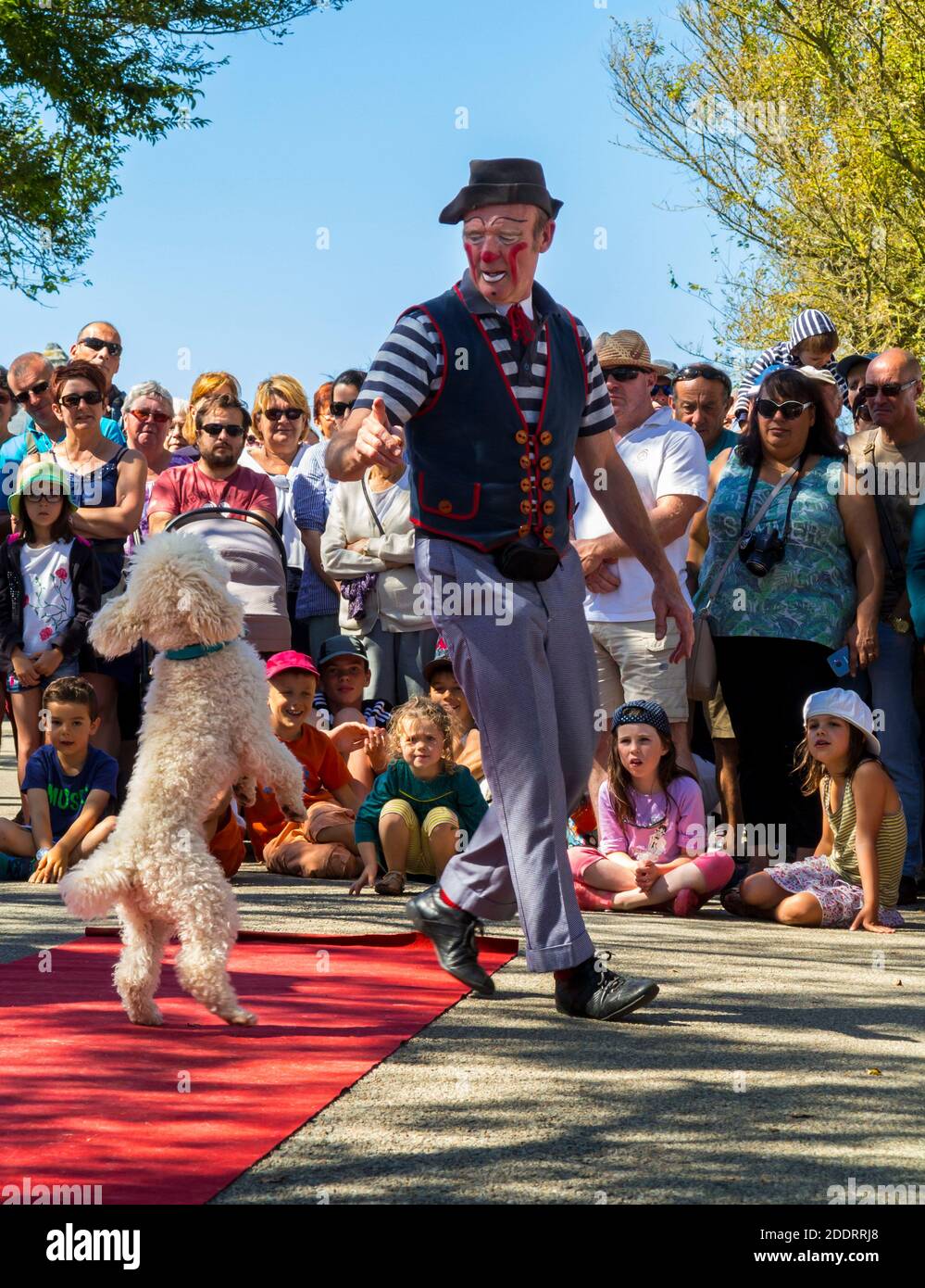 Traditional clown performing with a dog outside to a village crowd in ...