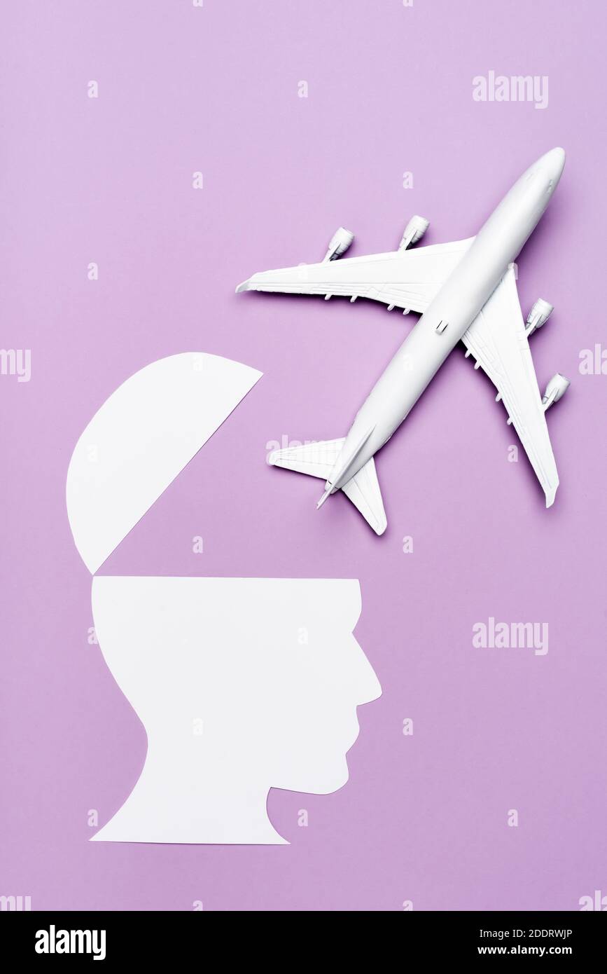 top view of white plane model and paper cut human head on violet ...