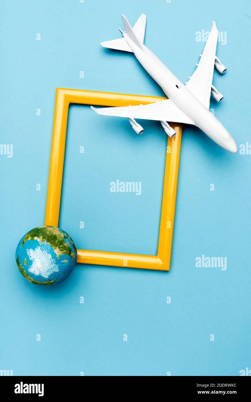 top view of white plane model, globe and empty frame on blue background ...