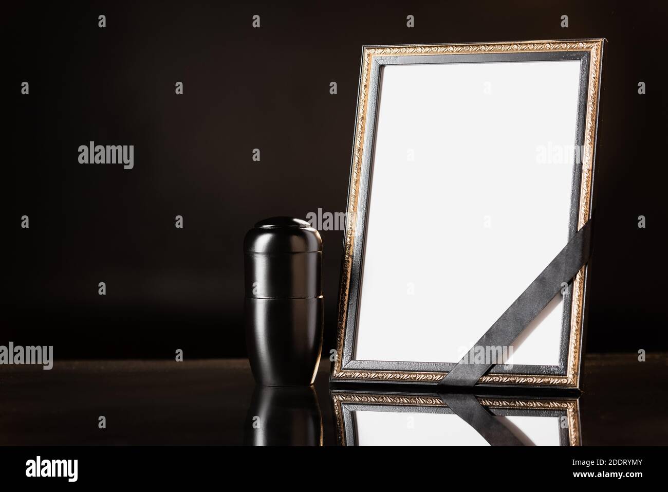urn with ashes, mirror with black ribbon on black background, funeral ...