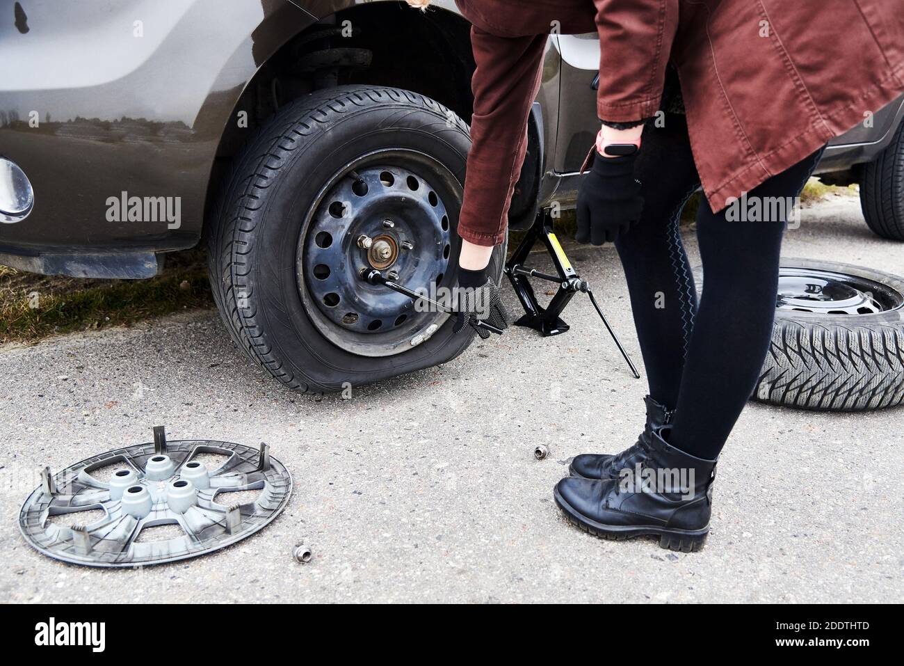 A young woman removes the wheel with a key near her car with a flat ...
