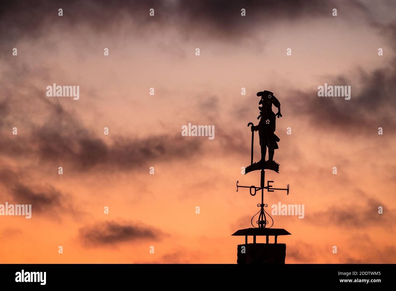 Wind vane in the shape of a cane man, silhouetted against a sunset sky ...