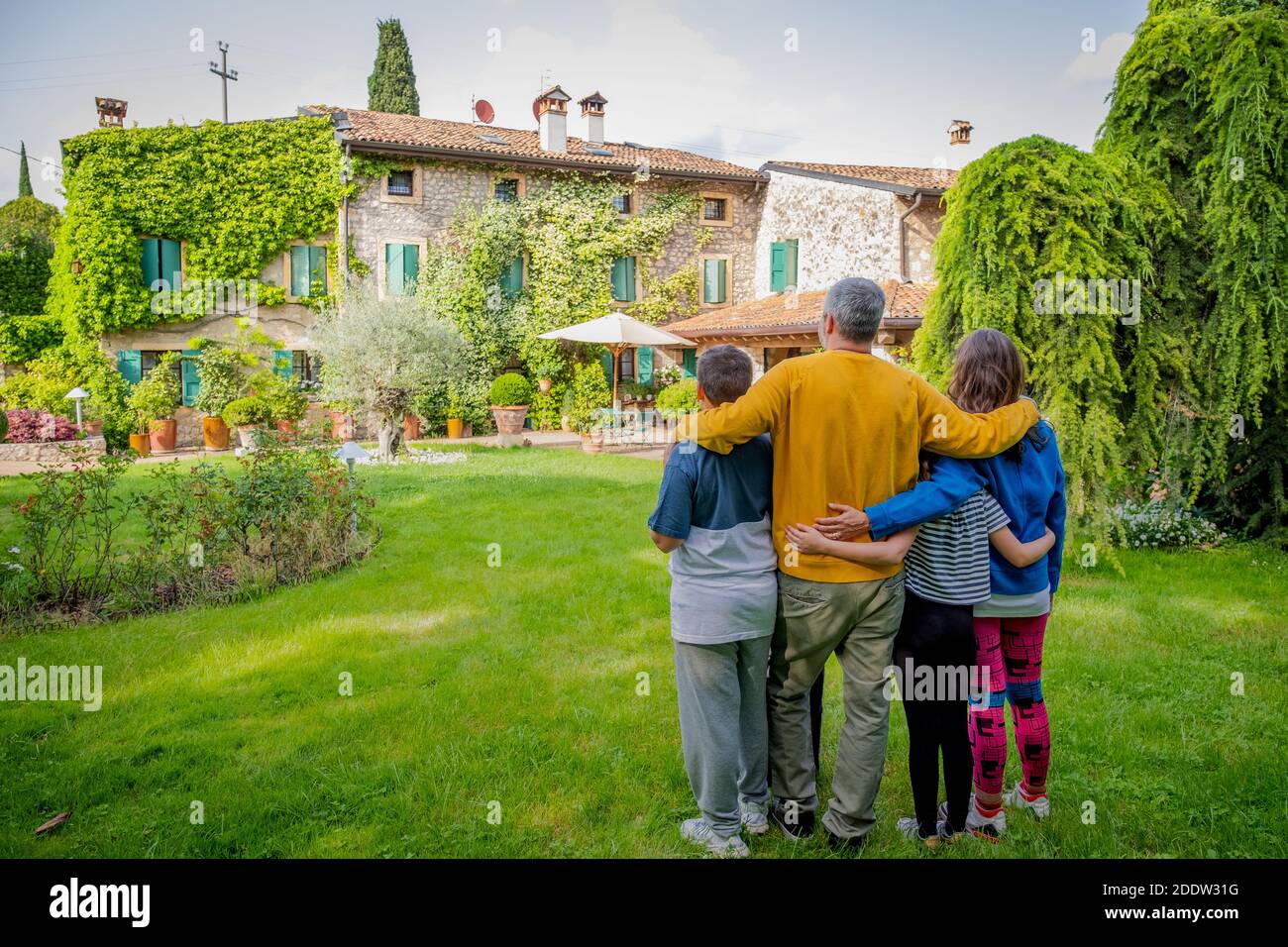 Back view of happy family hugging is standing outside their new house ...