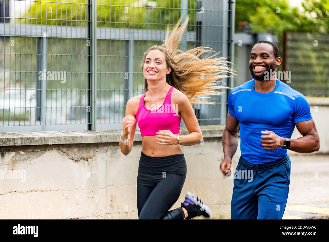 Young couple smiling to each other while jogging on the street, out to ...