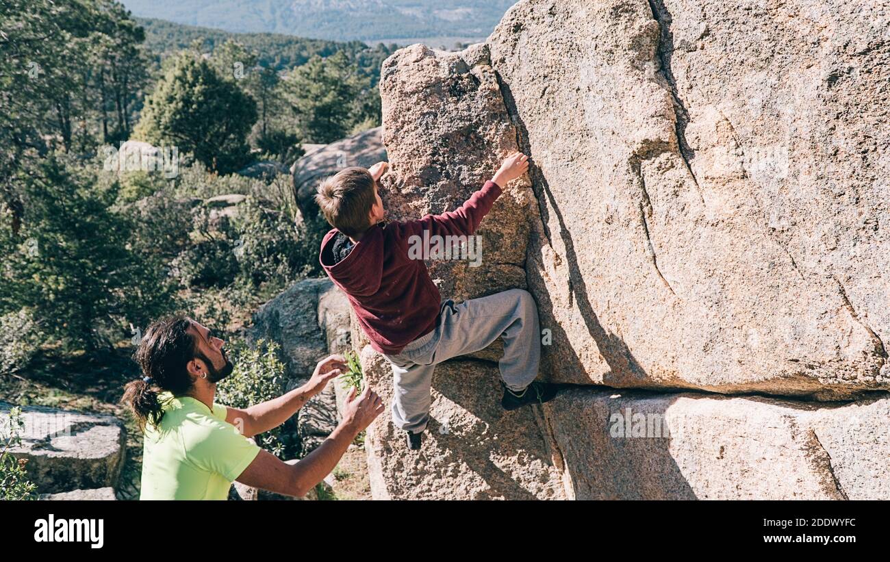 Stock photo of a man helping a young boy to climb a rock in the ...