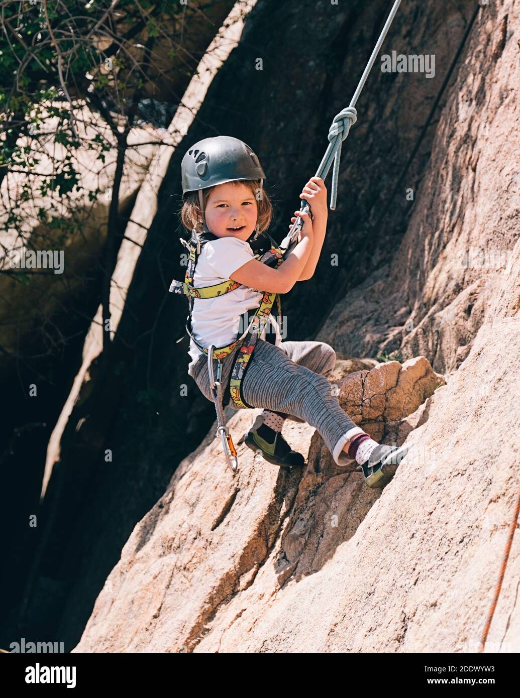Young girl smiling and having fun while she does rock climbing. She is ...