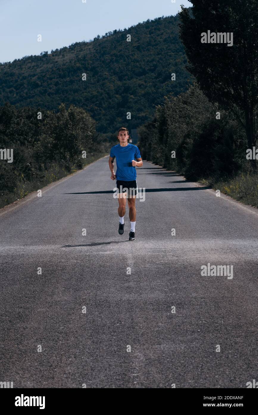 Male athlete running on an empty road in the woods while trying to get ...