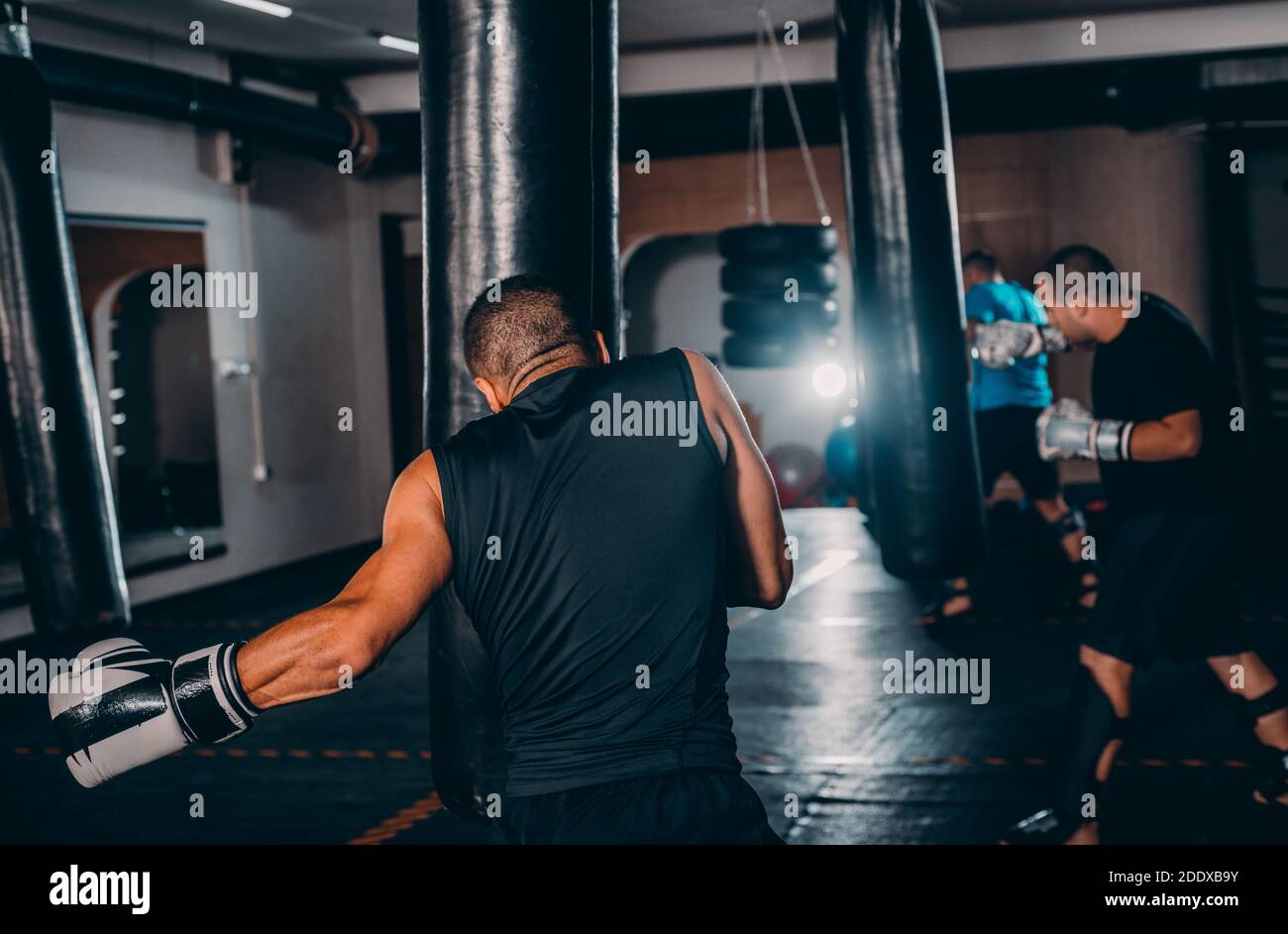 Strong kickboxer man punching black sand bag on gym background Stock ...