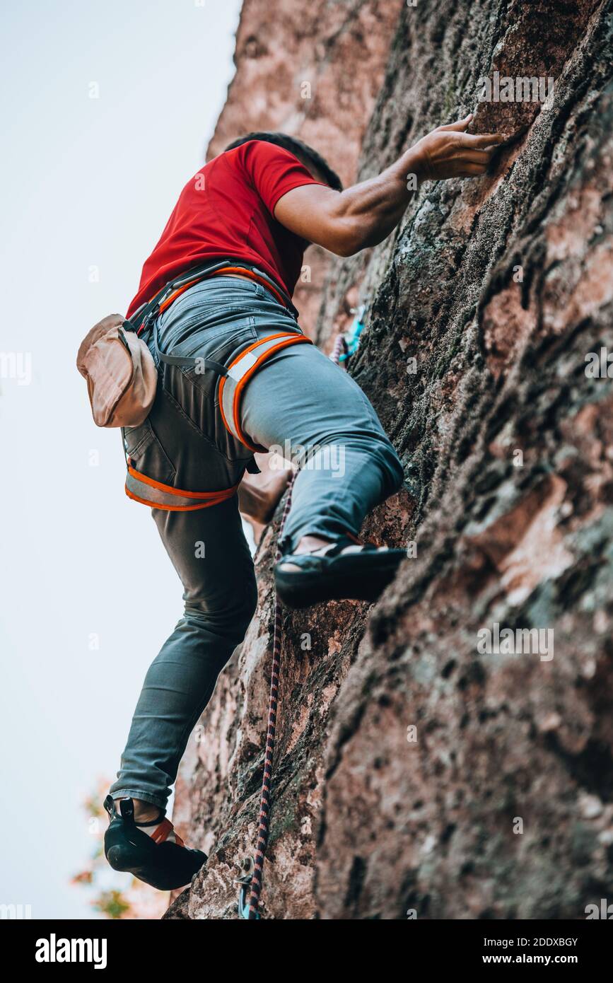 A man holding on to a piece of rock while he climbs up a steep cliff ...