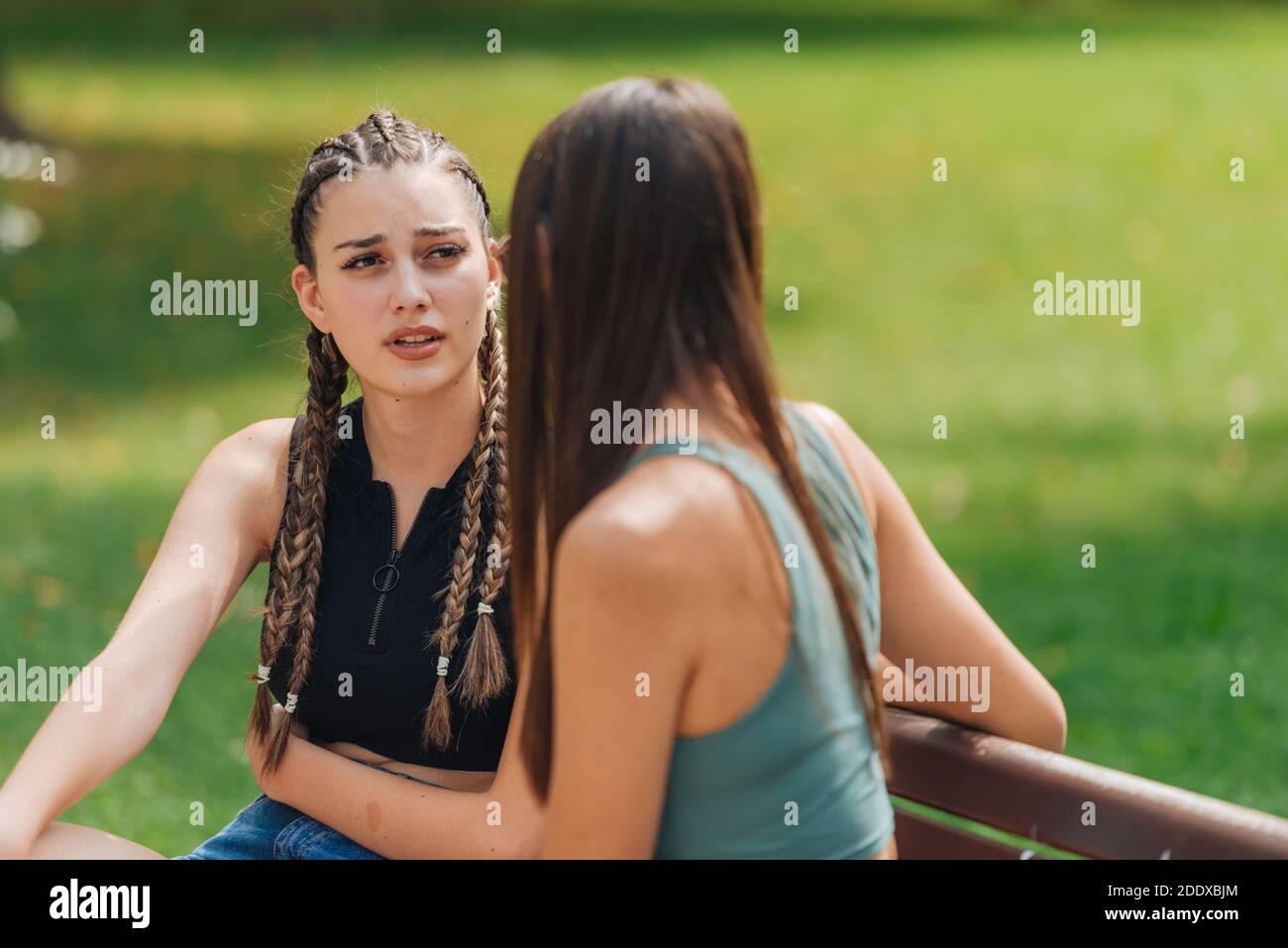 Two girls sitting on a bench in a park and talking to each other on a ...