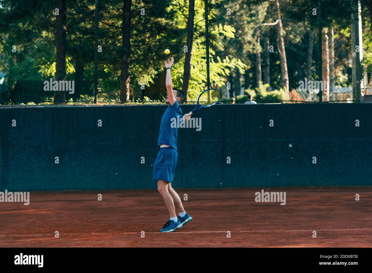 A professional tennis player is serving ball on a clay tennis court ...